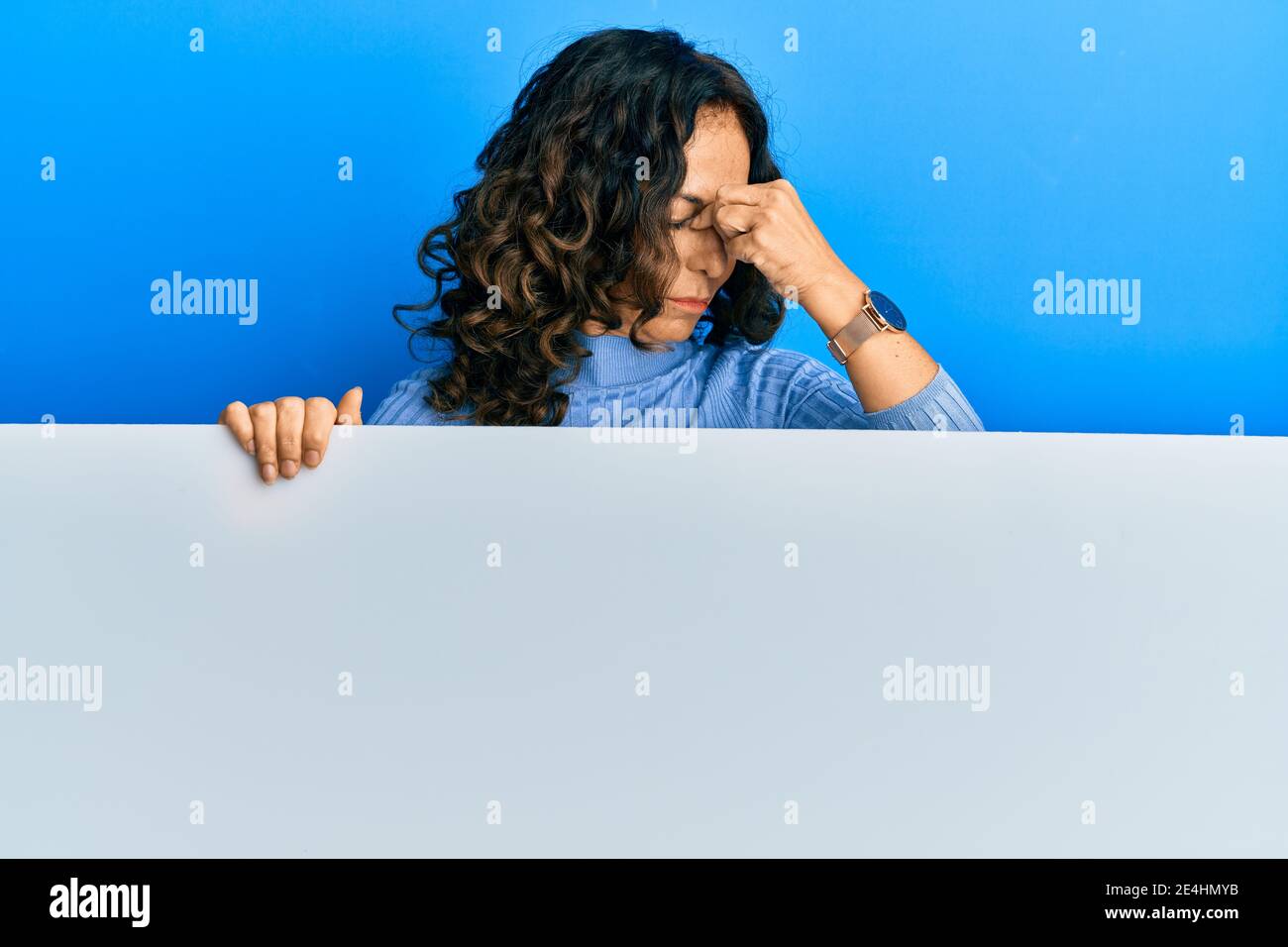 Middle age hispanic woman holding blank empty banner tired rubbing nose ...