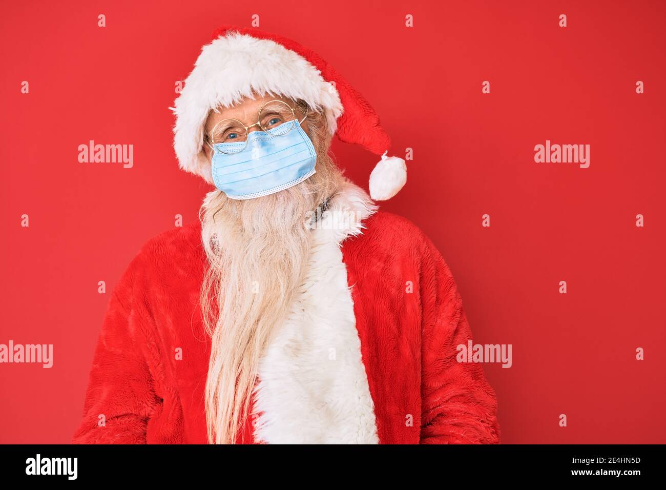 Old senior man wearing santa claus costume wearing safety mask with a ...