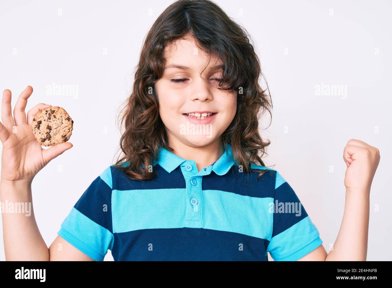 Cute hispanic child with long hair holding cookie screaming proud ...