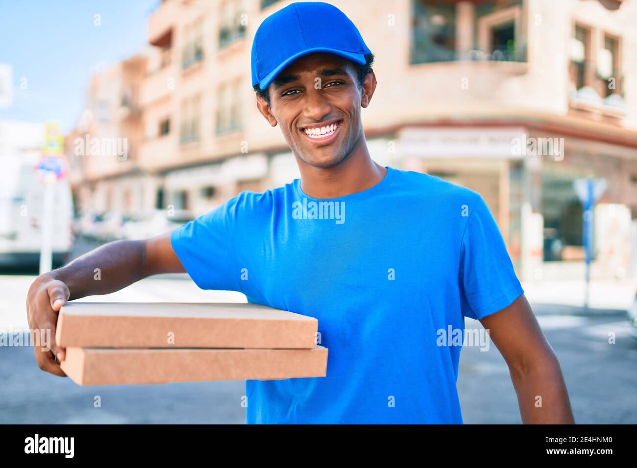 African delivery man wearing courier uniform outdoors holding take away ...