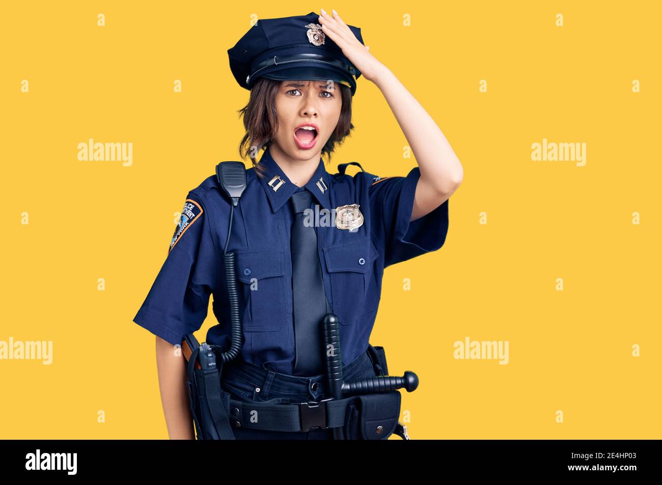 Young beautiful girl wearing police uniform surprised with hand on head ...