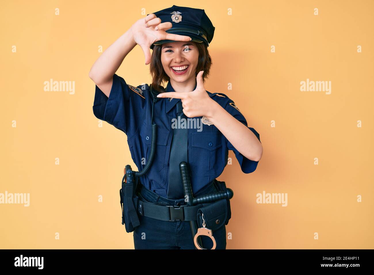 Young beautiful woman wearing police uniform smiling making frame with ...