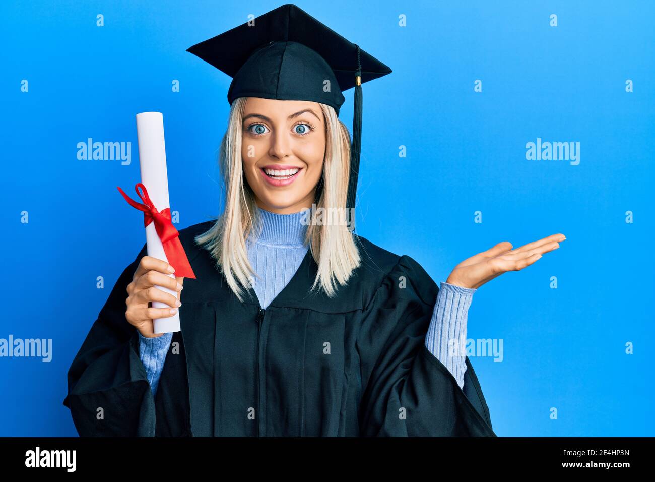 Beautiful blonde woman wearing graduation cap and ceremony robe holding ...