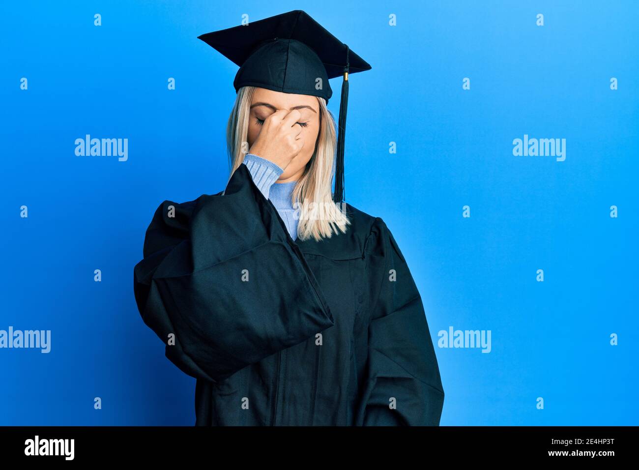 Beautiful blonde woman wearing graduation cap and ceremony robe tired ...