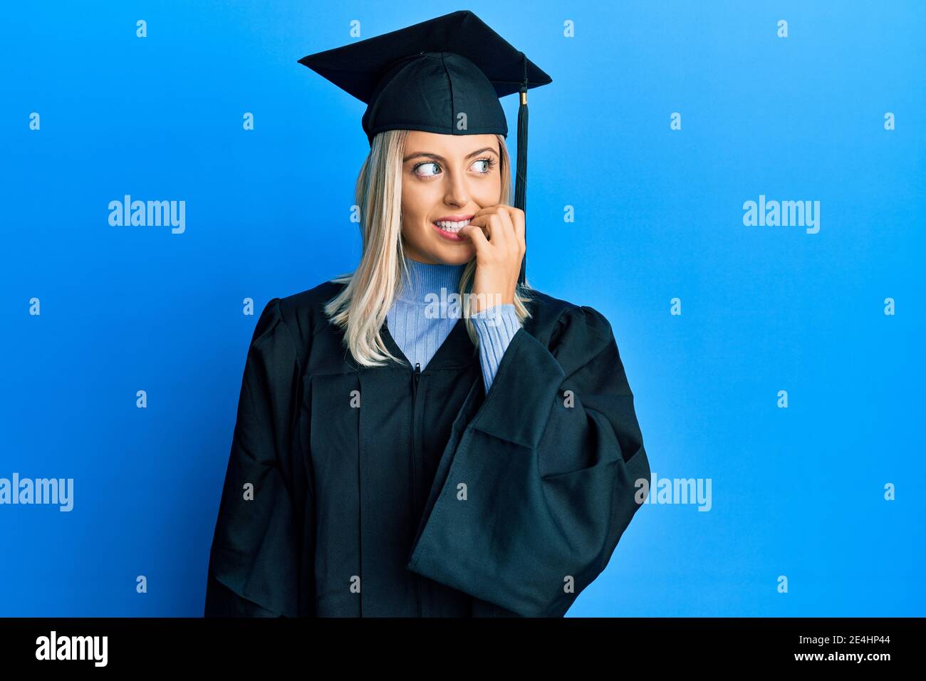 Beautiful blonde woman wearing graduation cap and ceremony robe looking ...