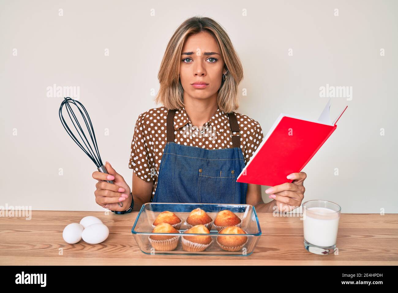 Beautiful caucasian woman wearing baker apron making muffins depressed ...