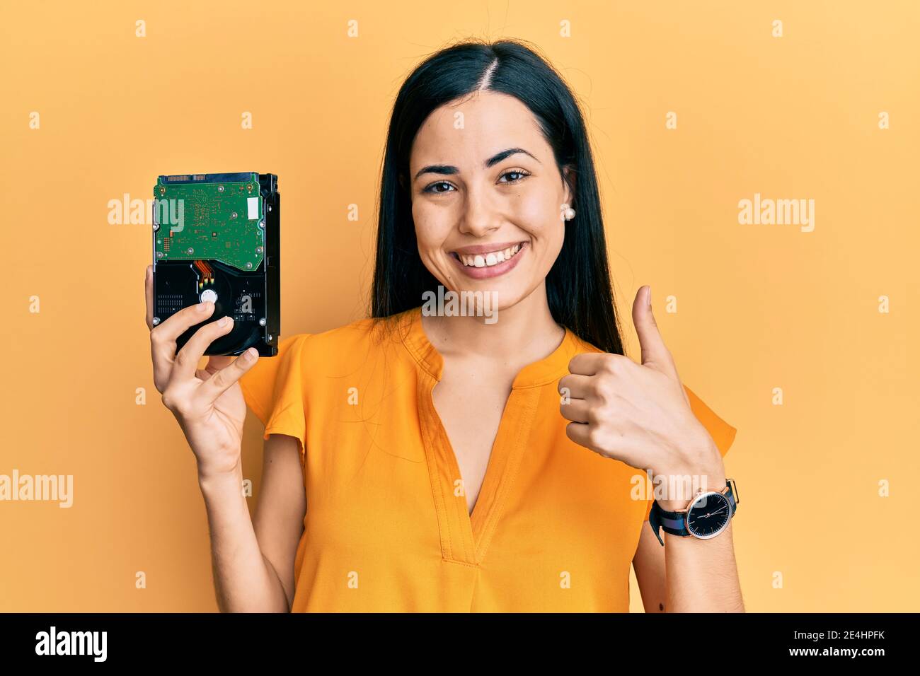 Beautiful young woman holding hard disk smiling happy and positive ...