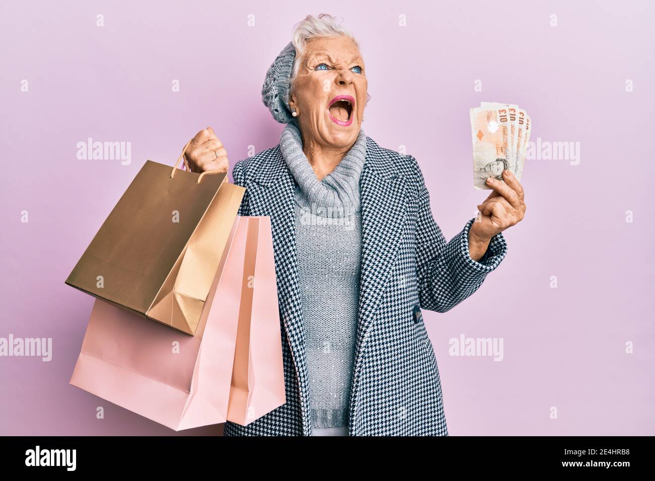 Senior grey-haired woman holding shopping bags and uk pounds banknotes ...