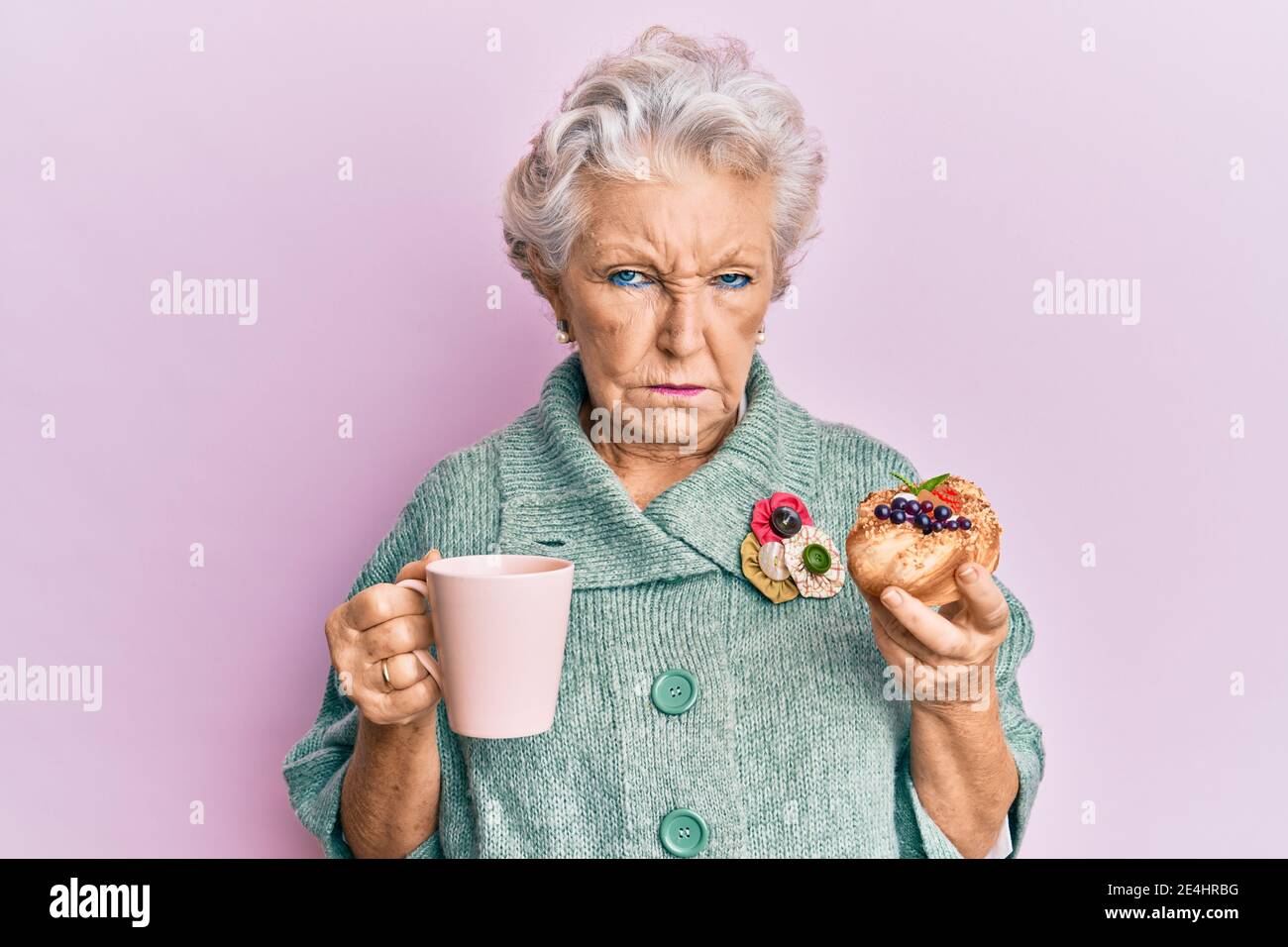 Senior grey-haired woman drinking a cup of coffee and eating bun ...