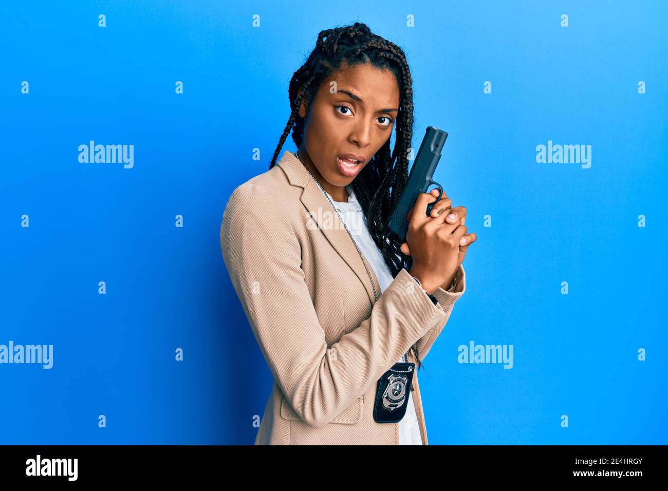 African american police woman holding gun in shock face, looking ...