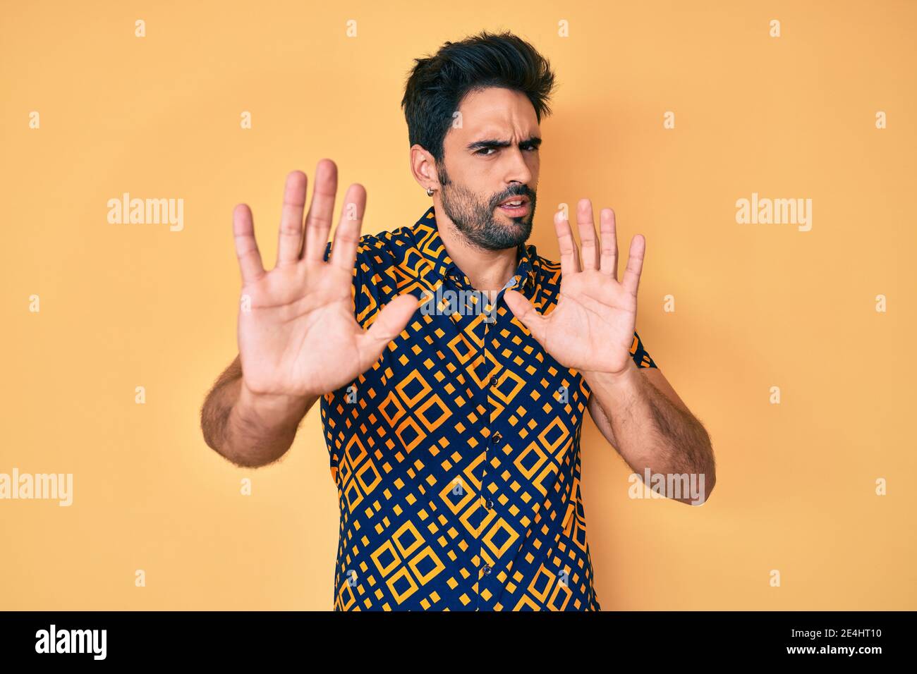 Handsome hispanic man with beard wearing 80s disco style shirt afraid ...