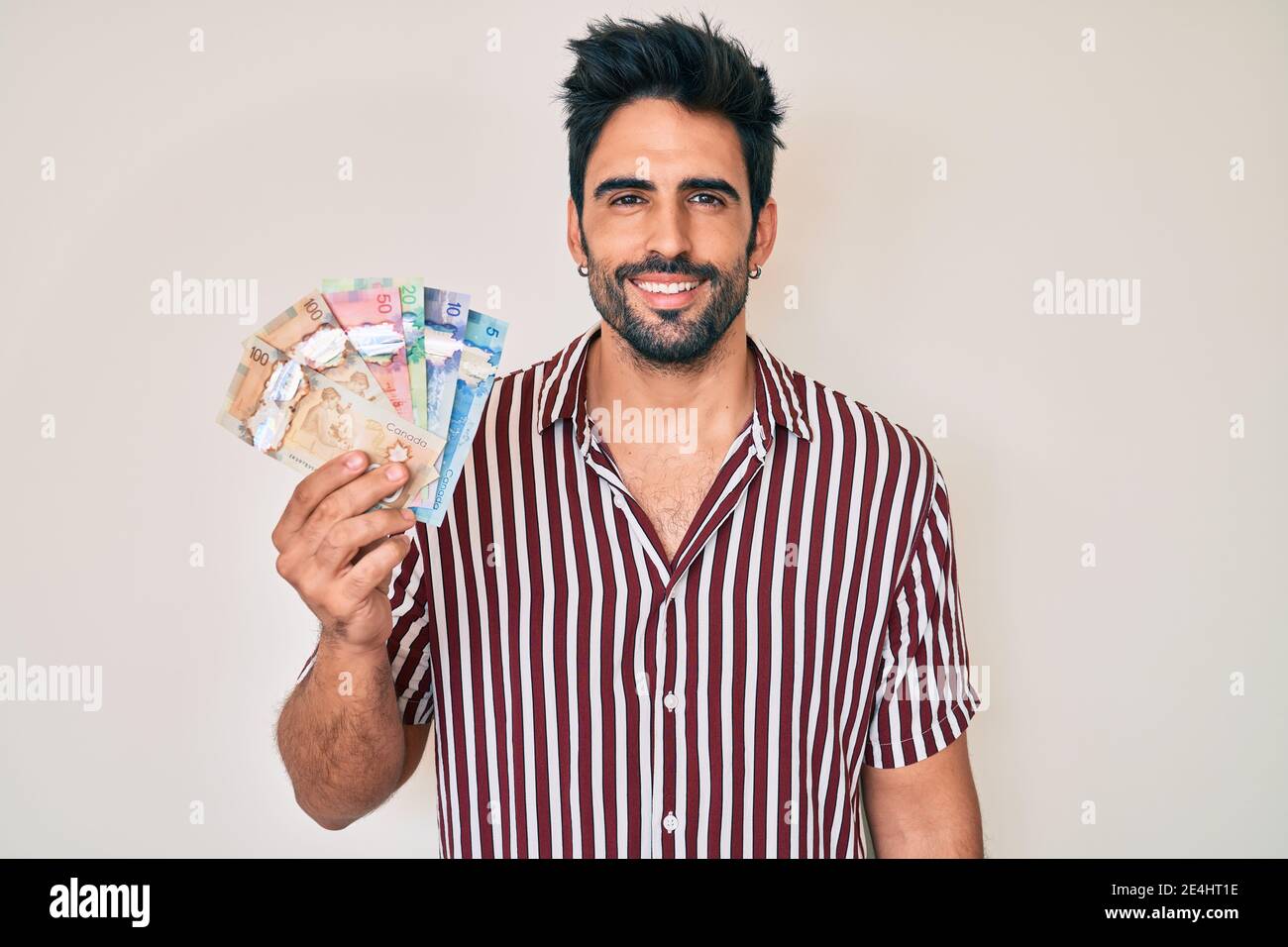 Handsome hispanic man with beard holding canadian dollars looking ...