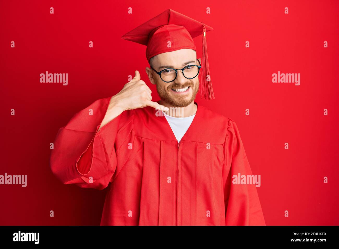 Young redhead man wearing red graduation cap and ceremony robe smiling ...