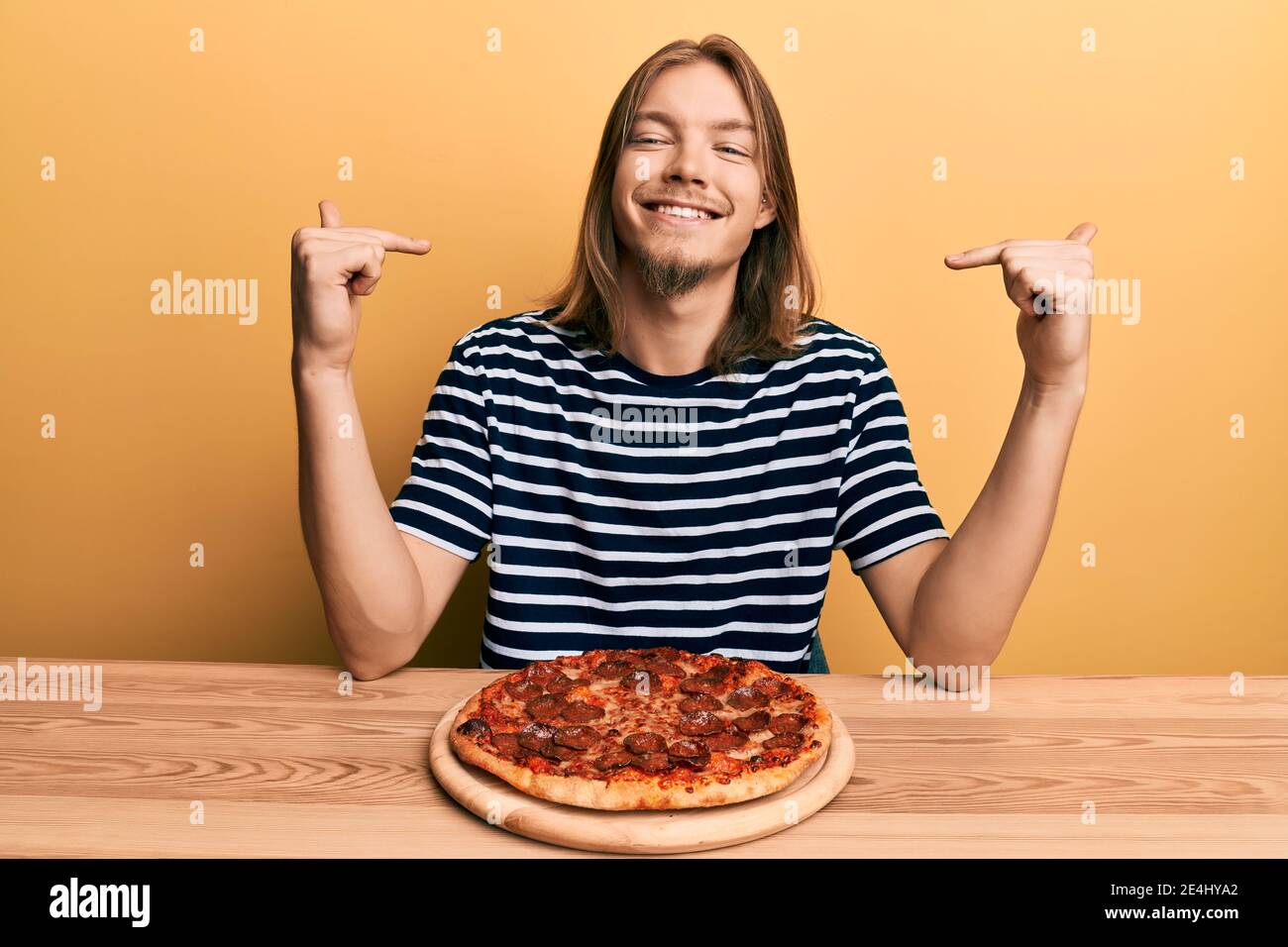Handsome caucasian man with long hair eating tasty pepperoni pizza ...