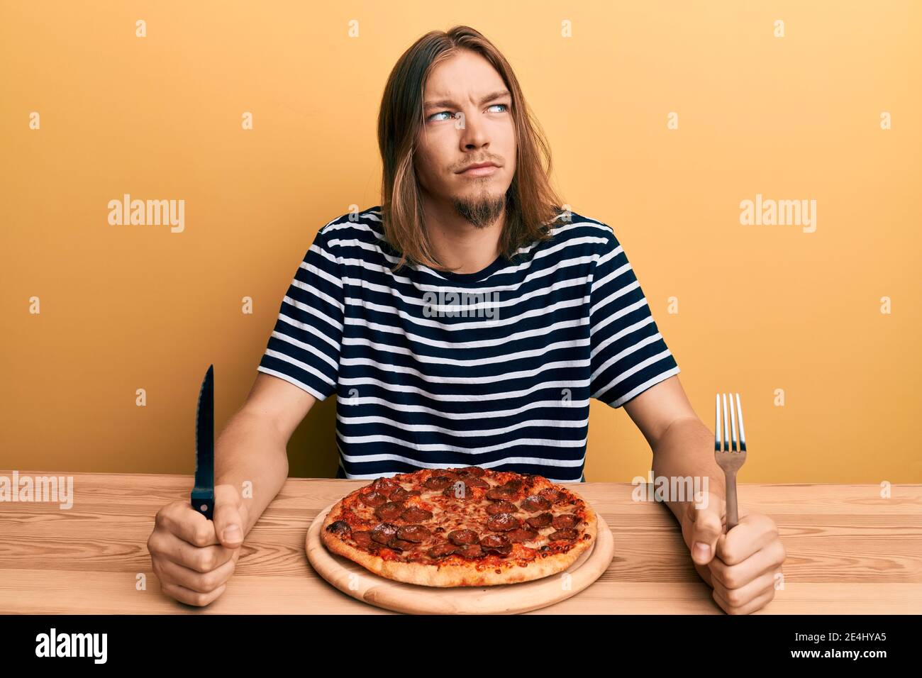 Handsome caucasian man with long hair eating tasty pepperoni pizza ...