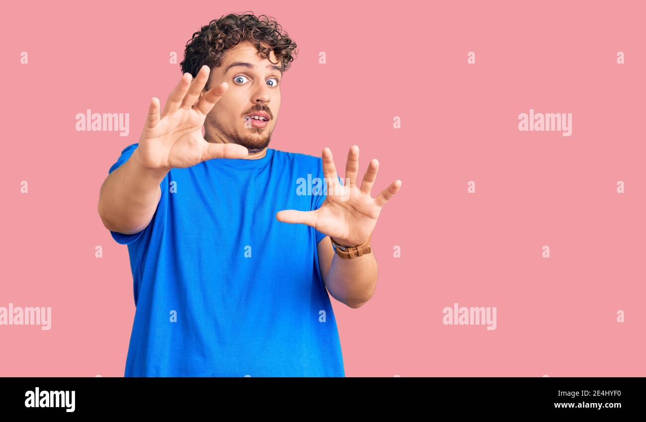 Young handsome man with curly hair wearing casual clothes afraid and ...