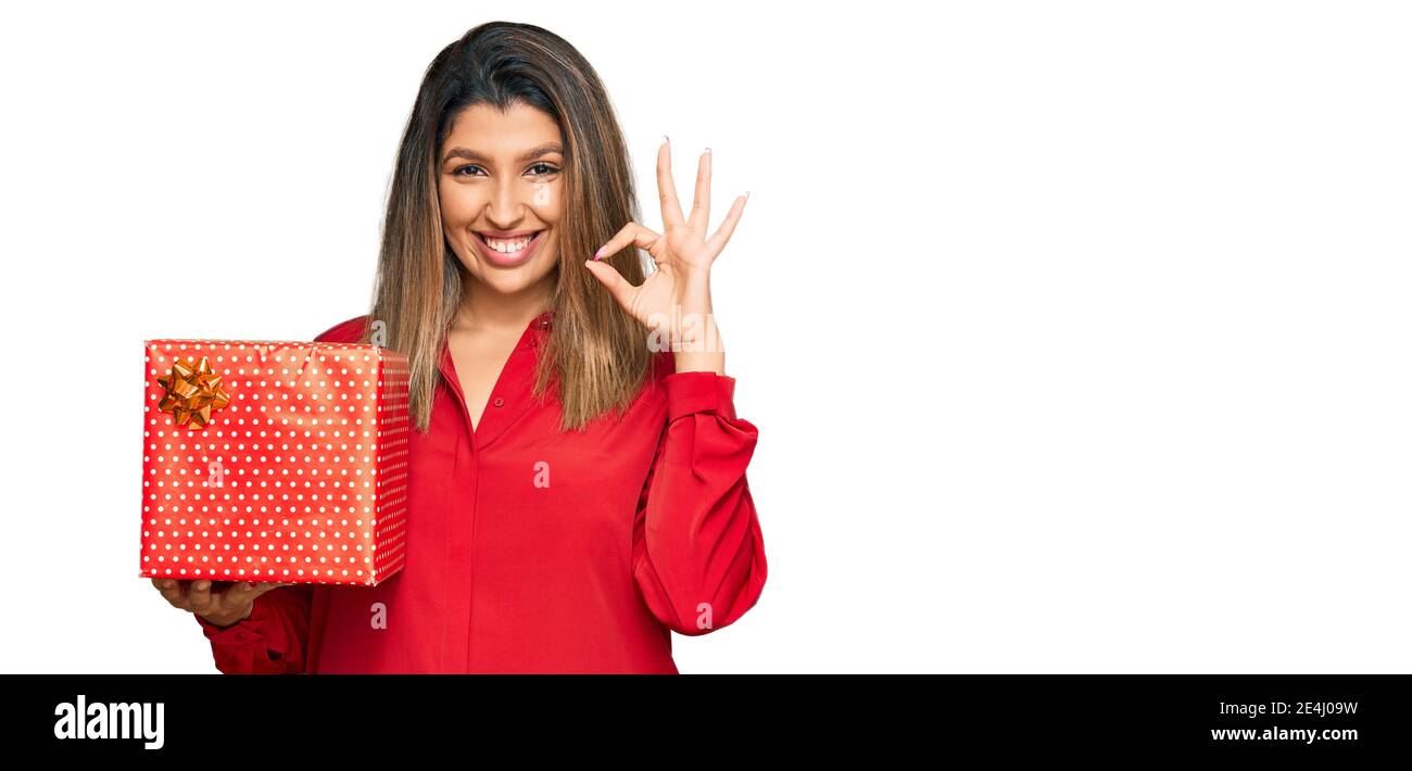 Beautiful brunette woman holding gift doing ok sign with fingers ...