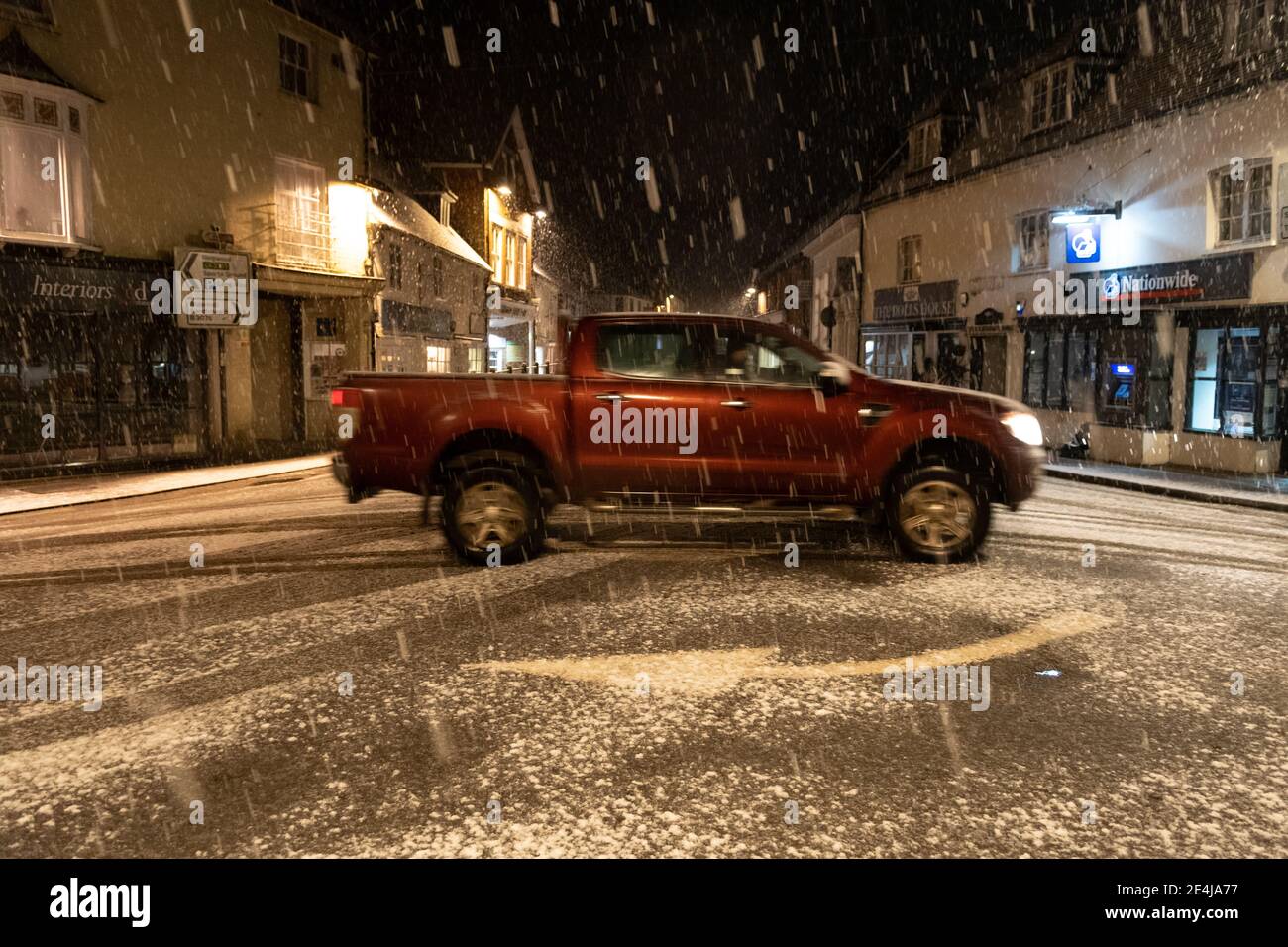 Falling snow on high street at night. Driving car in snow around mini ...