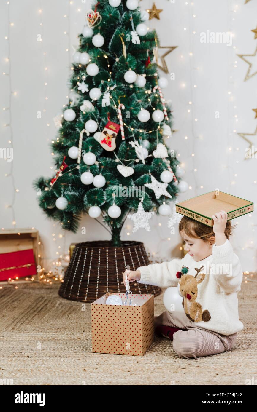 Baby girl with gift box sitting by Christmas tree at home Stock Photo ...