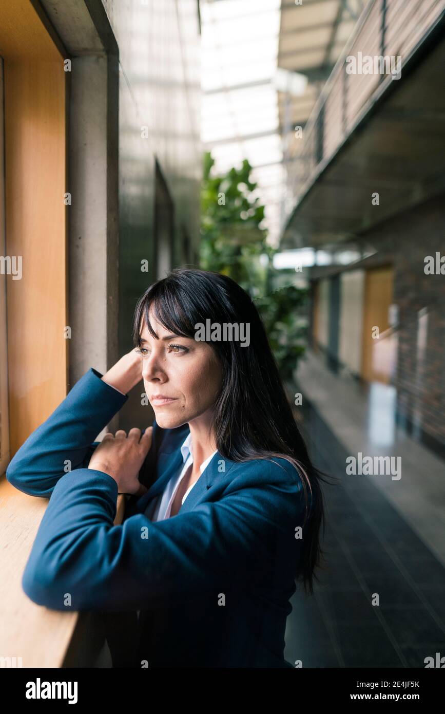 Thoughtful businesswoman leaning on window in corridor Stock Photo - Alamy