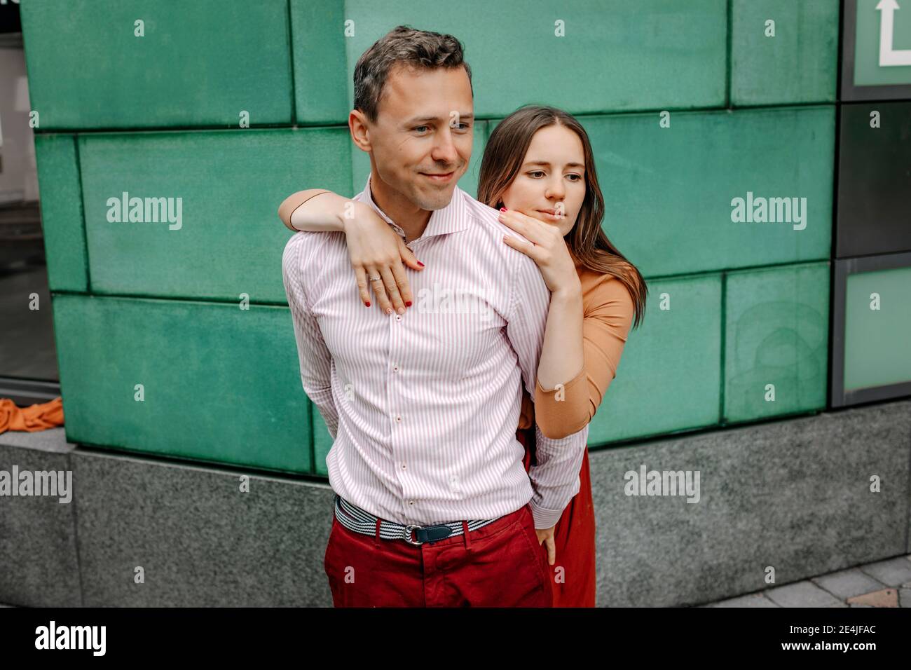 Girlfriend embracing boyfriend from back against green wall Stock Photo ...