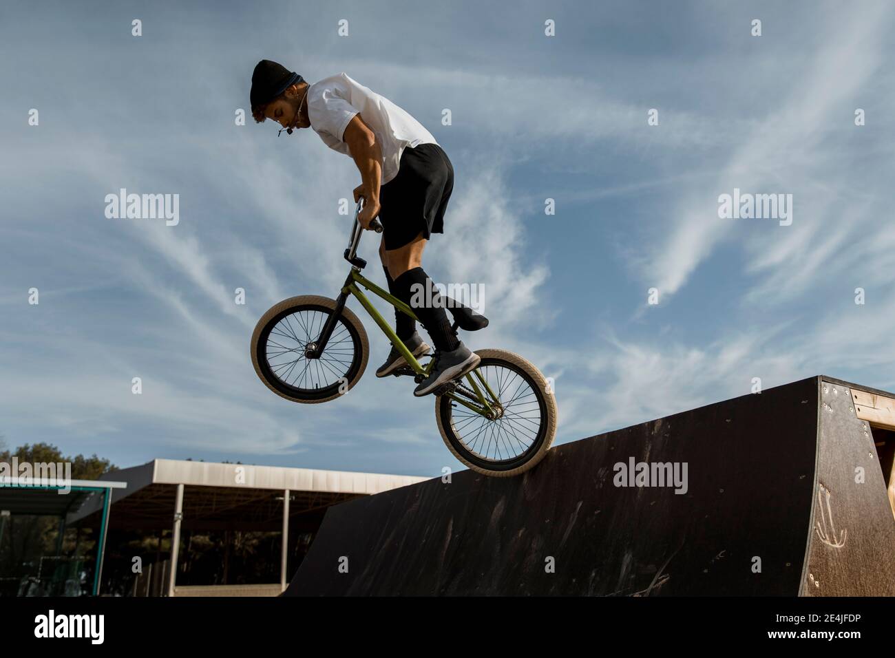 Young man jumping on ramp at bike park against sky Stock Photo - Alamy