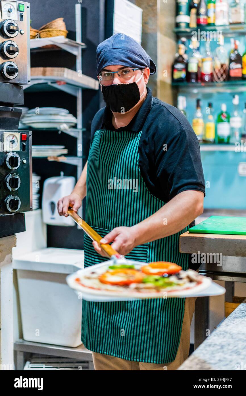 Portrait of male chef wearing protective face mask holding peel with ...