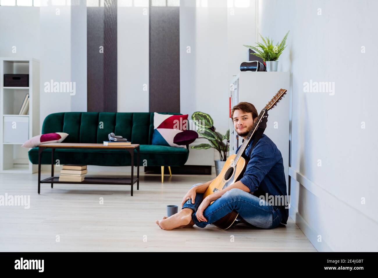 Musician smiling while sitting with guitar on floor at studio Stock ...