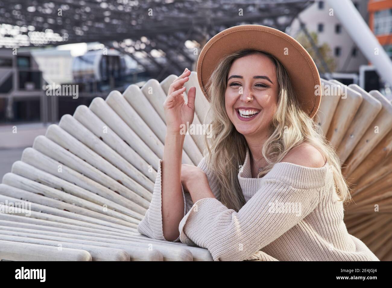 Cheerful young woman wearing hat standing by patterned retaining wall ...