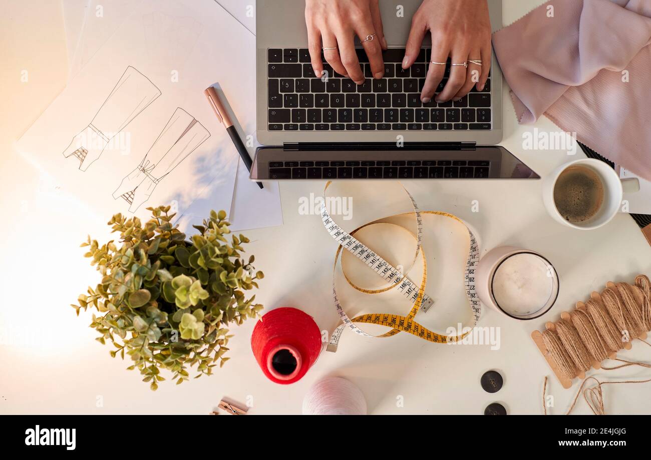 Fashion designer using laptop by fabric swatch and coffee at desk in ...
