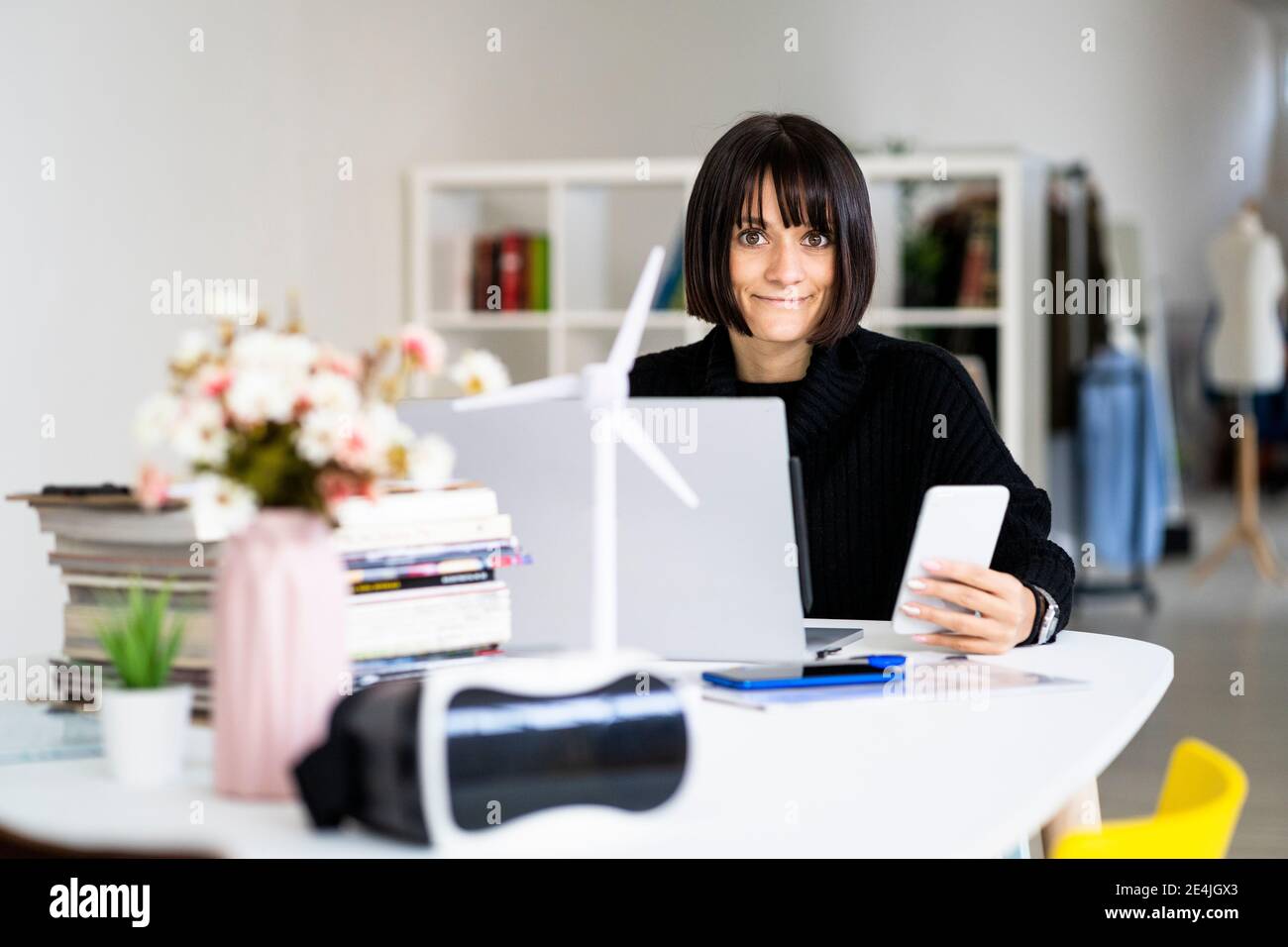 Young woman with laptop holding mobile phone while studying in study ...