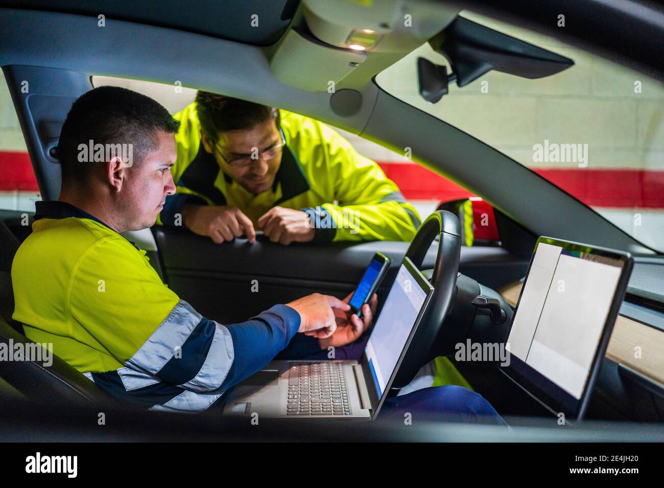 Male programmer showing mobile phone to colleague while sitting in ...
