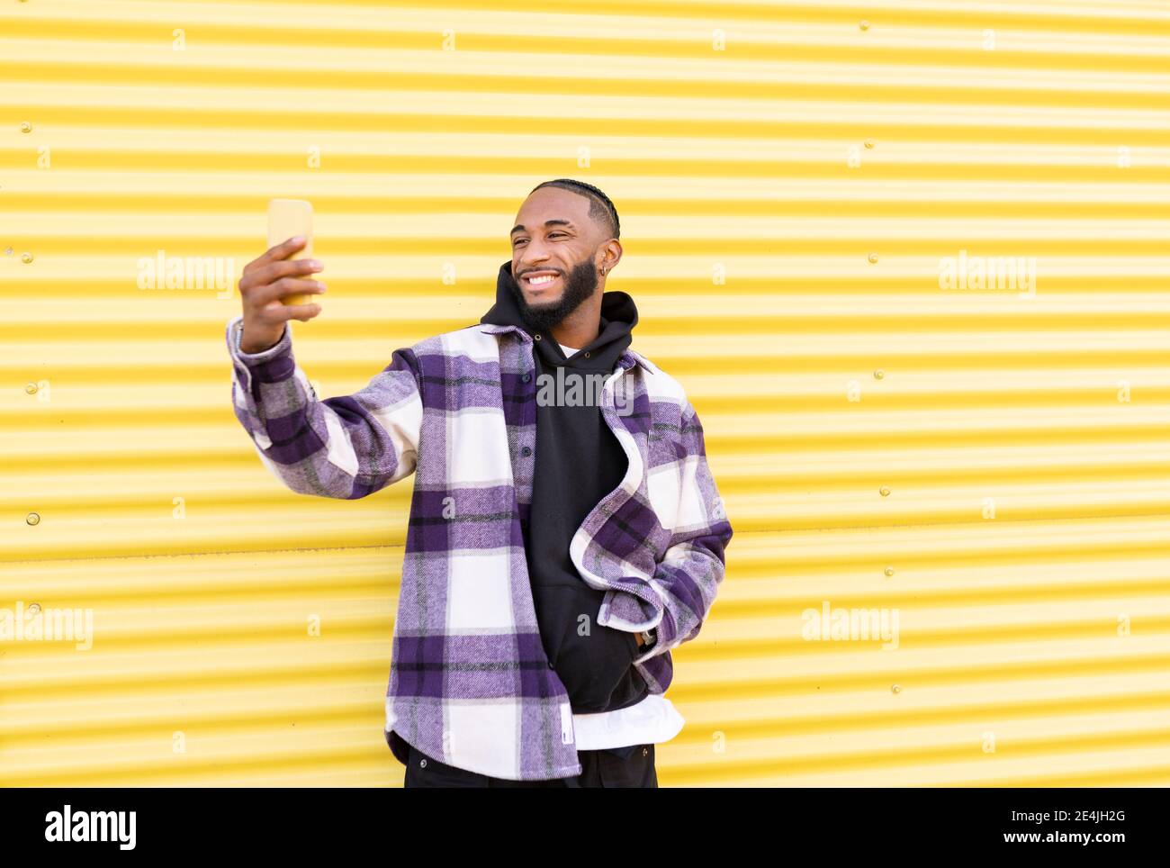 Male rapper taking selfie through mobile phone while smiling against ...