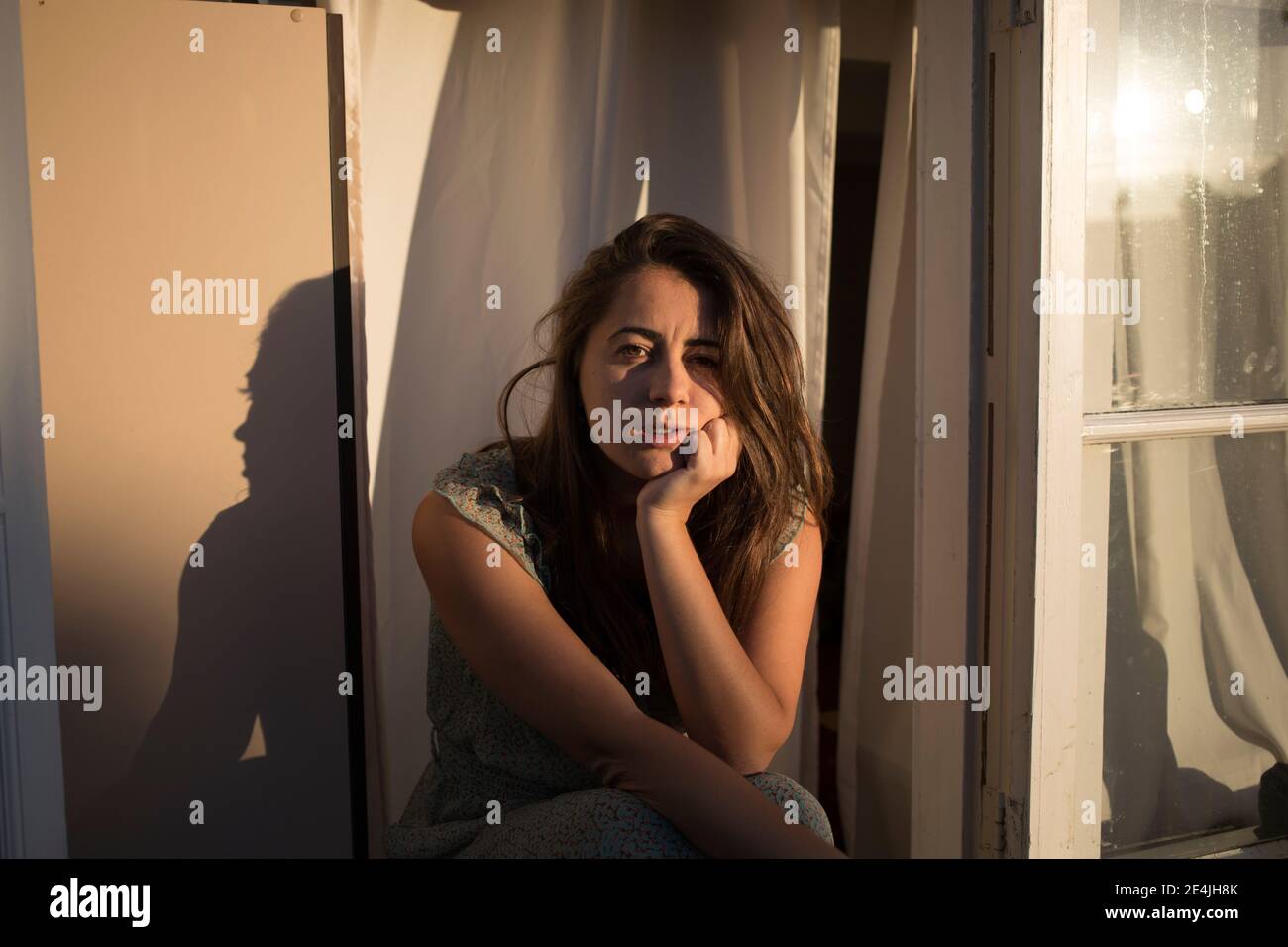 Beautiful woman with hand on chin sitting over window of house Stock ...