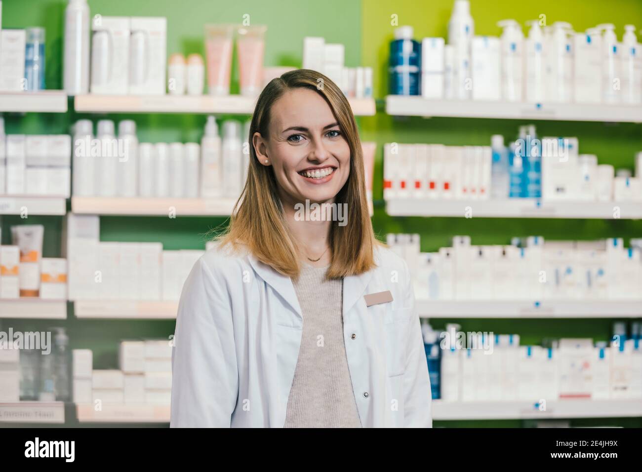 Confident pharmacist wearing lab coat while standing in chemist shop ...