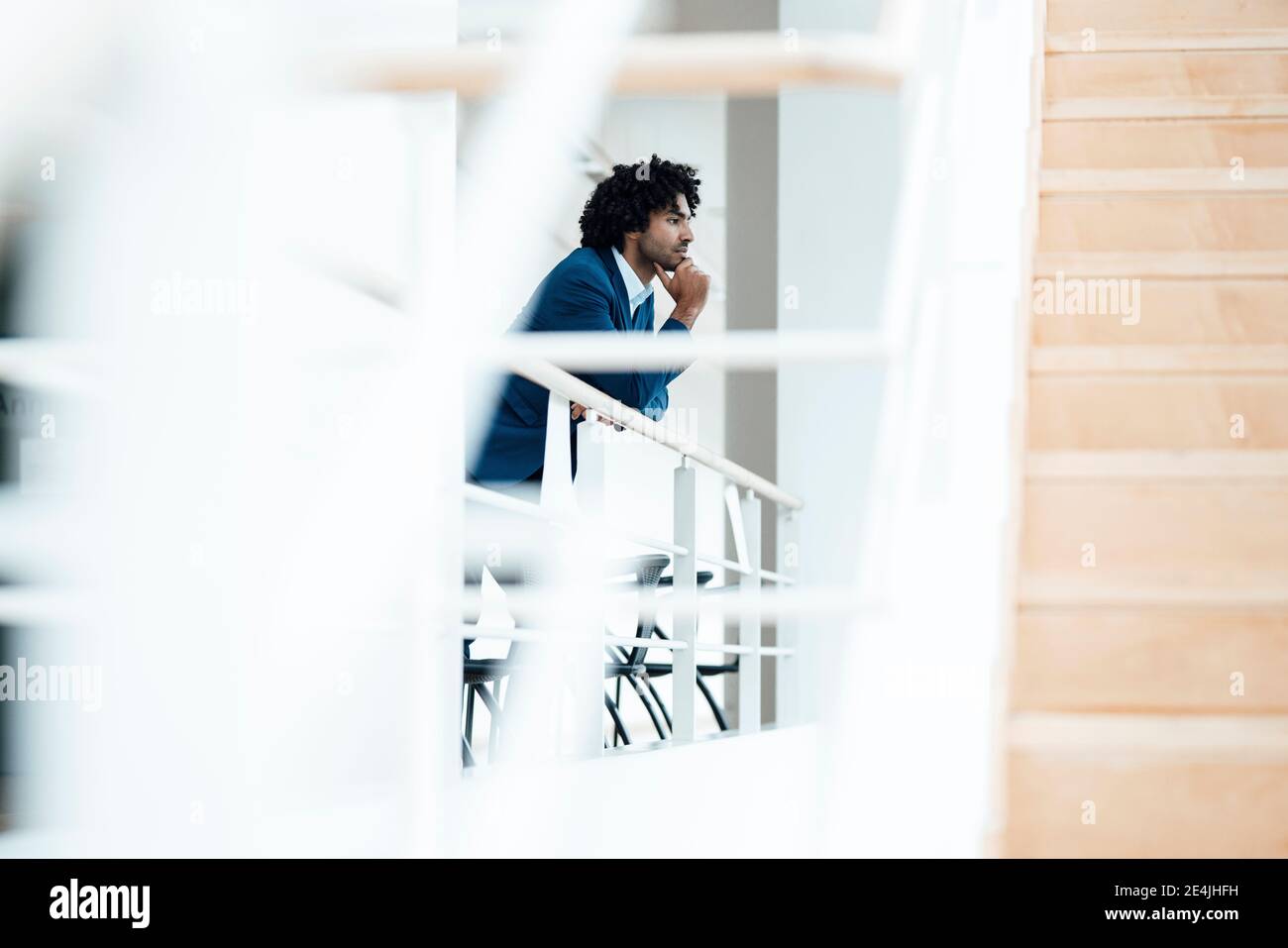 Thoughtful businessman leaning on railing by staircase in office Stock ...