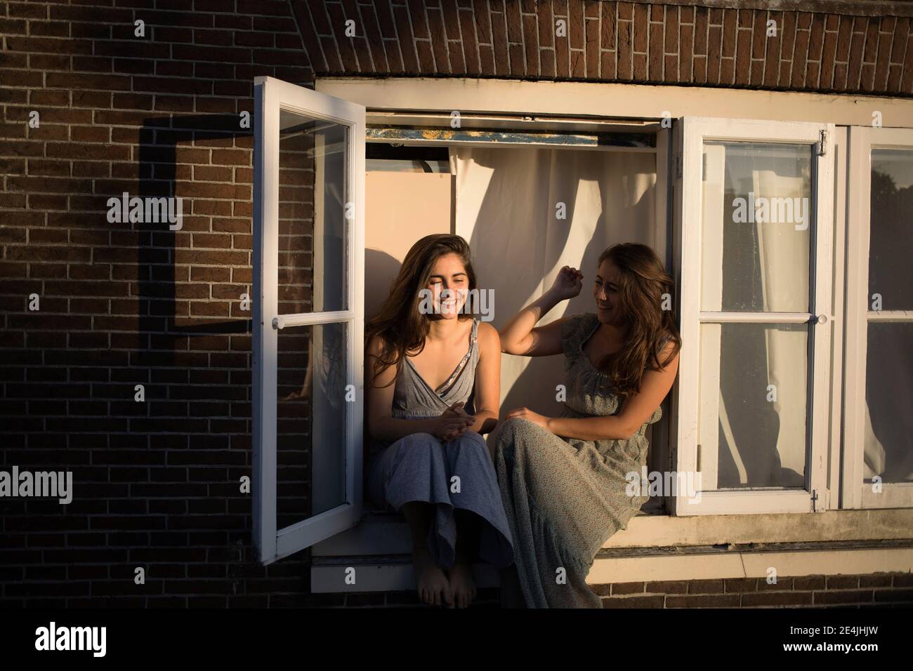 Female friends talking while sitting on window during sunset Stock ...