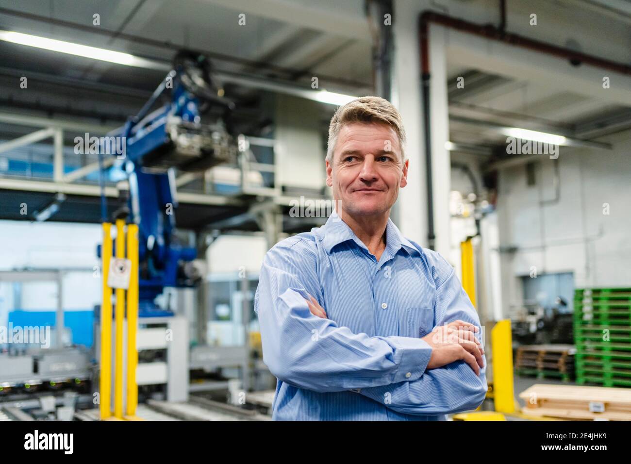 Smiling supervisor with arms crossed looking away in industry Stock ...