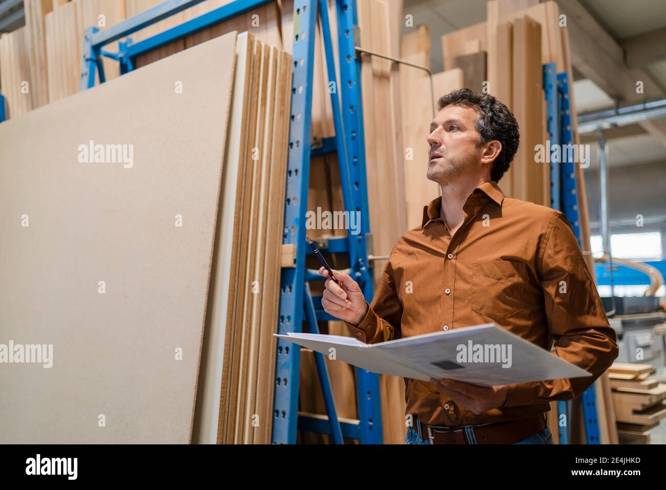 Portrait of carpenter standing with ring binder in front of shelves ...