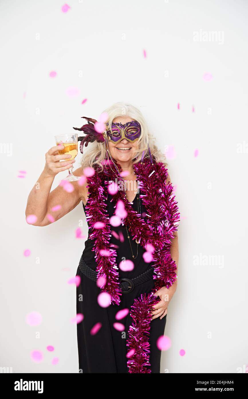 Happy fashionable senior woman with glass wearing masquerade mask ...