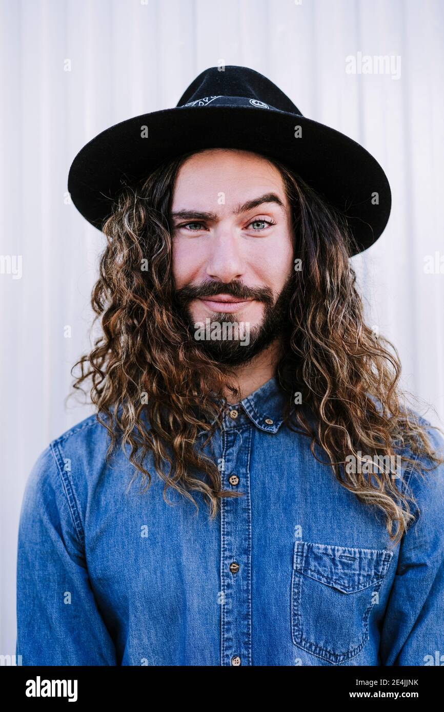 Handsome young man with raised eyebrow wearing hat against wall Stock ...