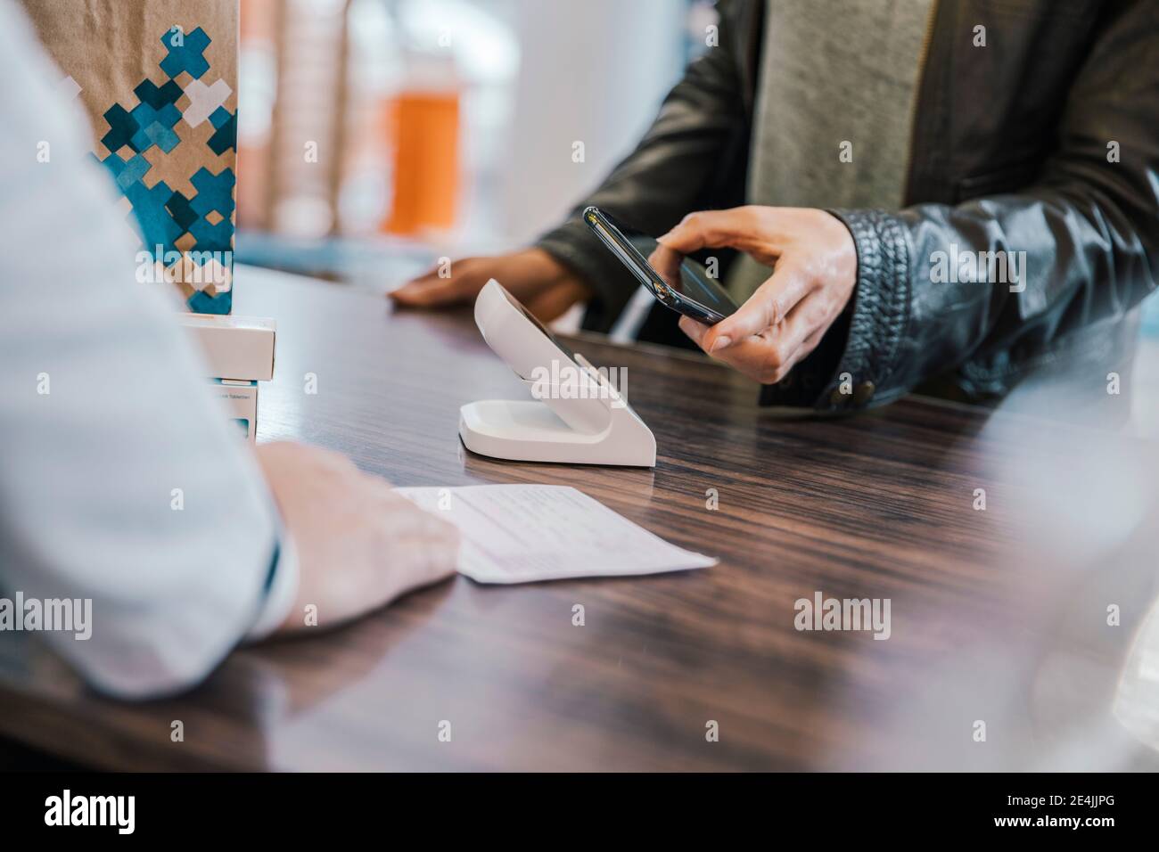 Midsection of customer with mobile phone at checkout counter in chemist ...