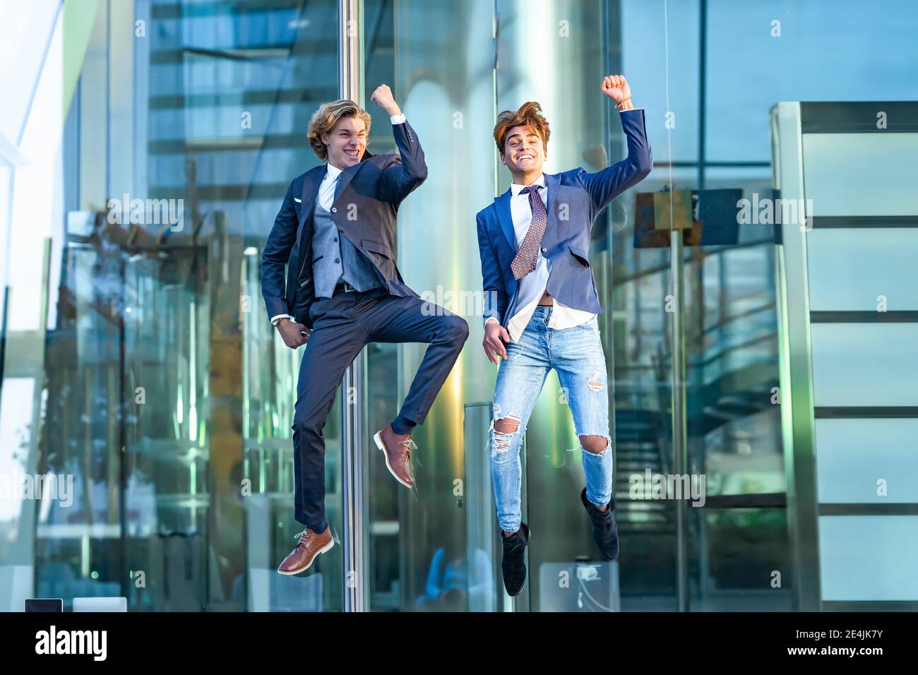 Cheerful male colleagues jumping against glass office building Stock ...