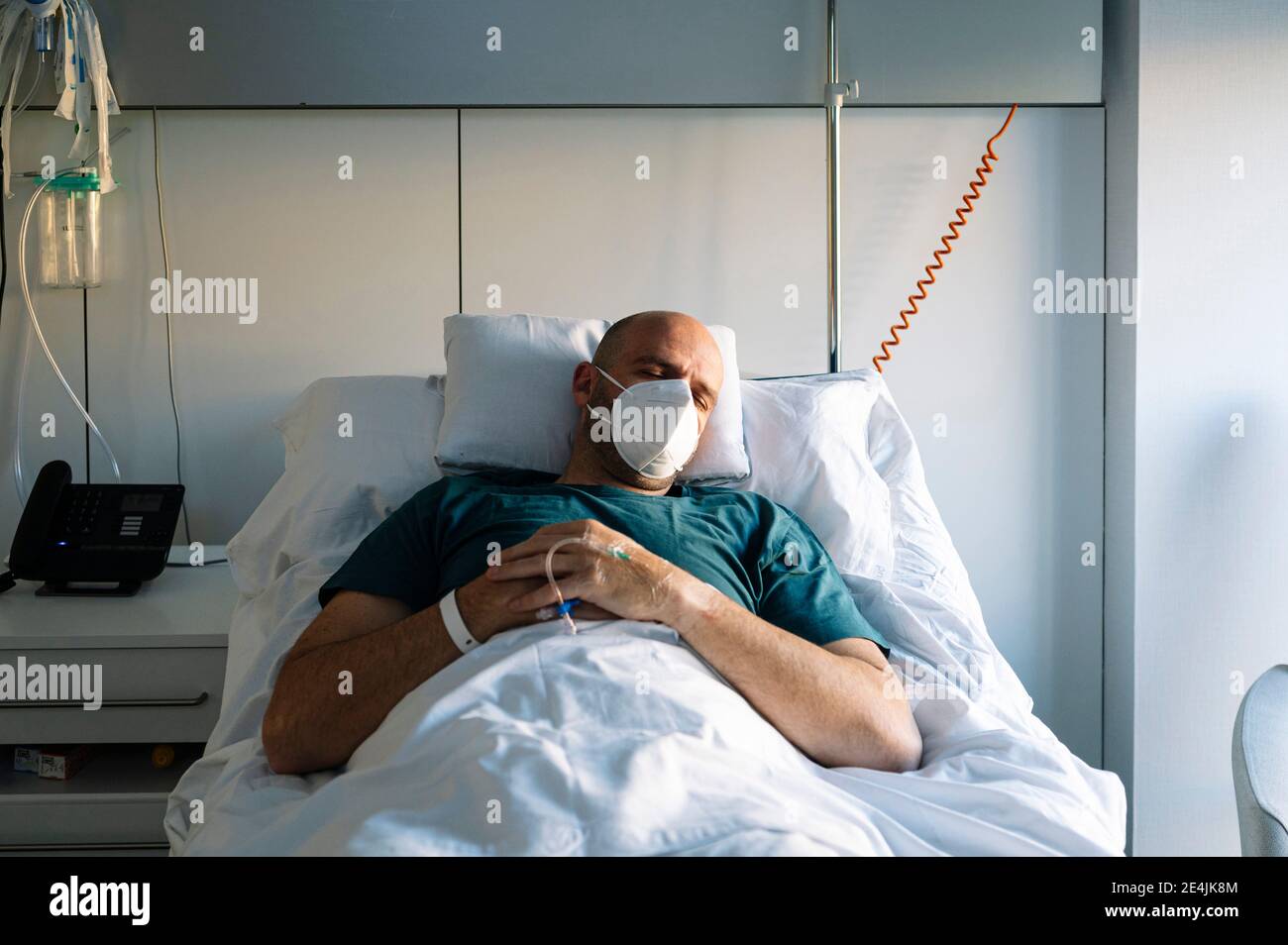 Patient wearing protective face mask using mobile phone while lying on ...
