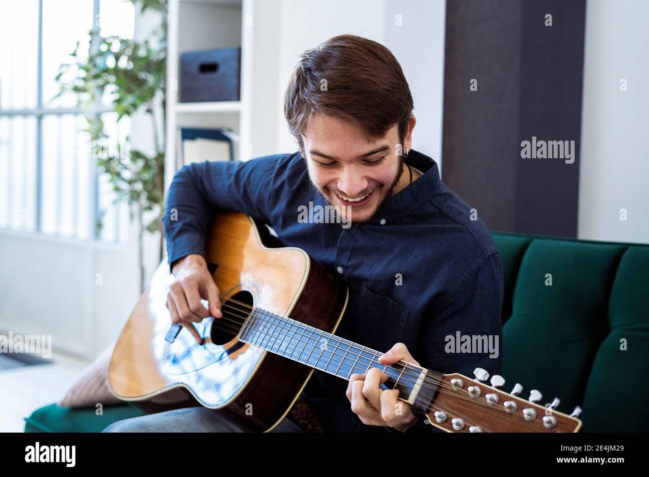 Smiling guitarist playing guitar while sitting on sofa at studio Stock ...