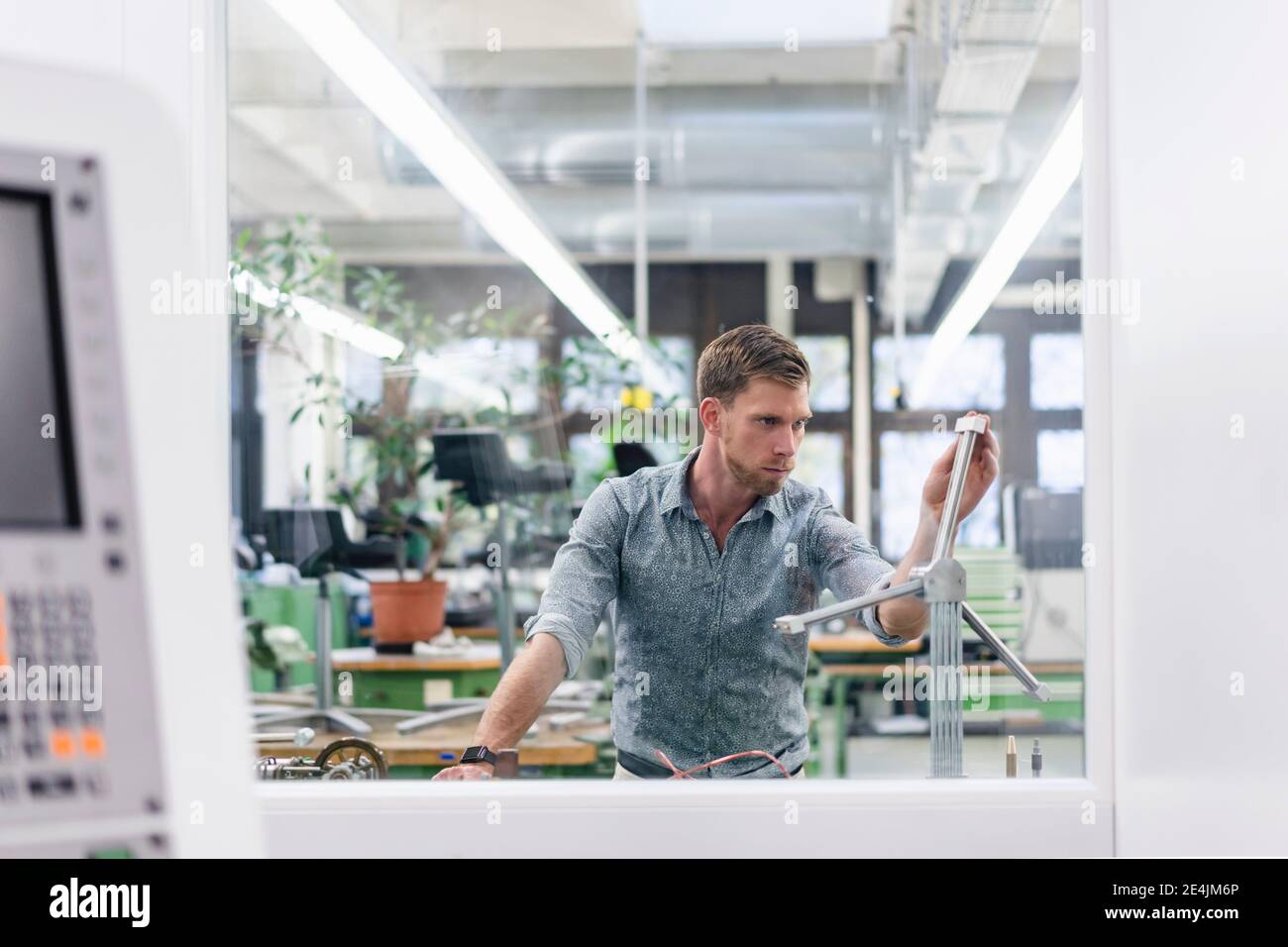 Male engineer examining wind turbine seen through glass in factory ...