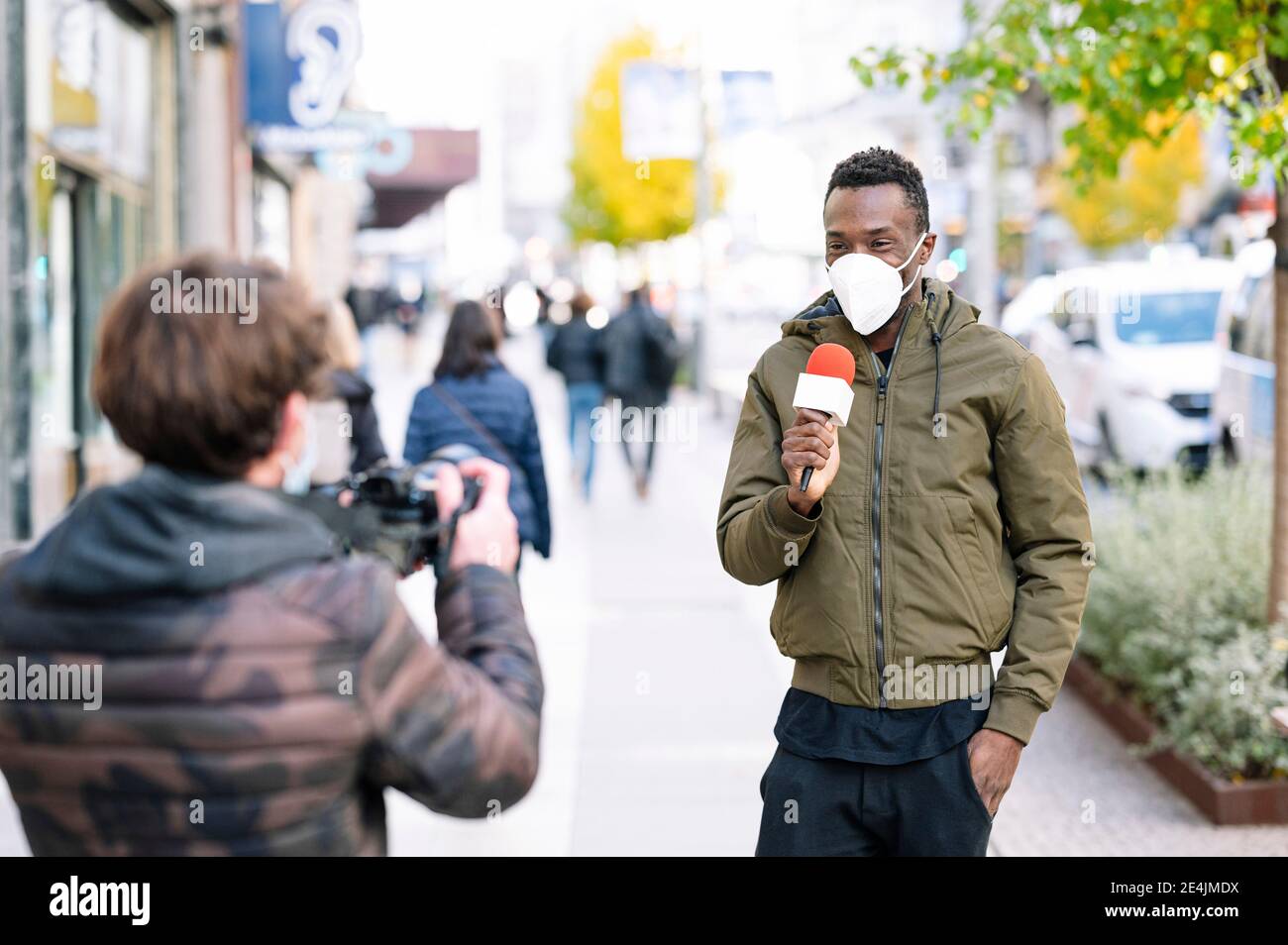 Man filming reporter talking over microphone while standing on street ...