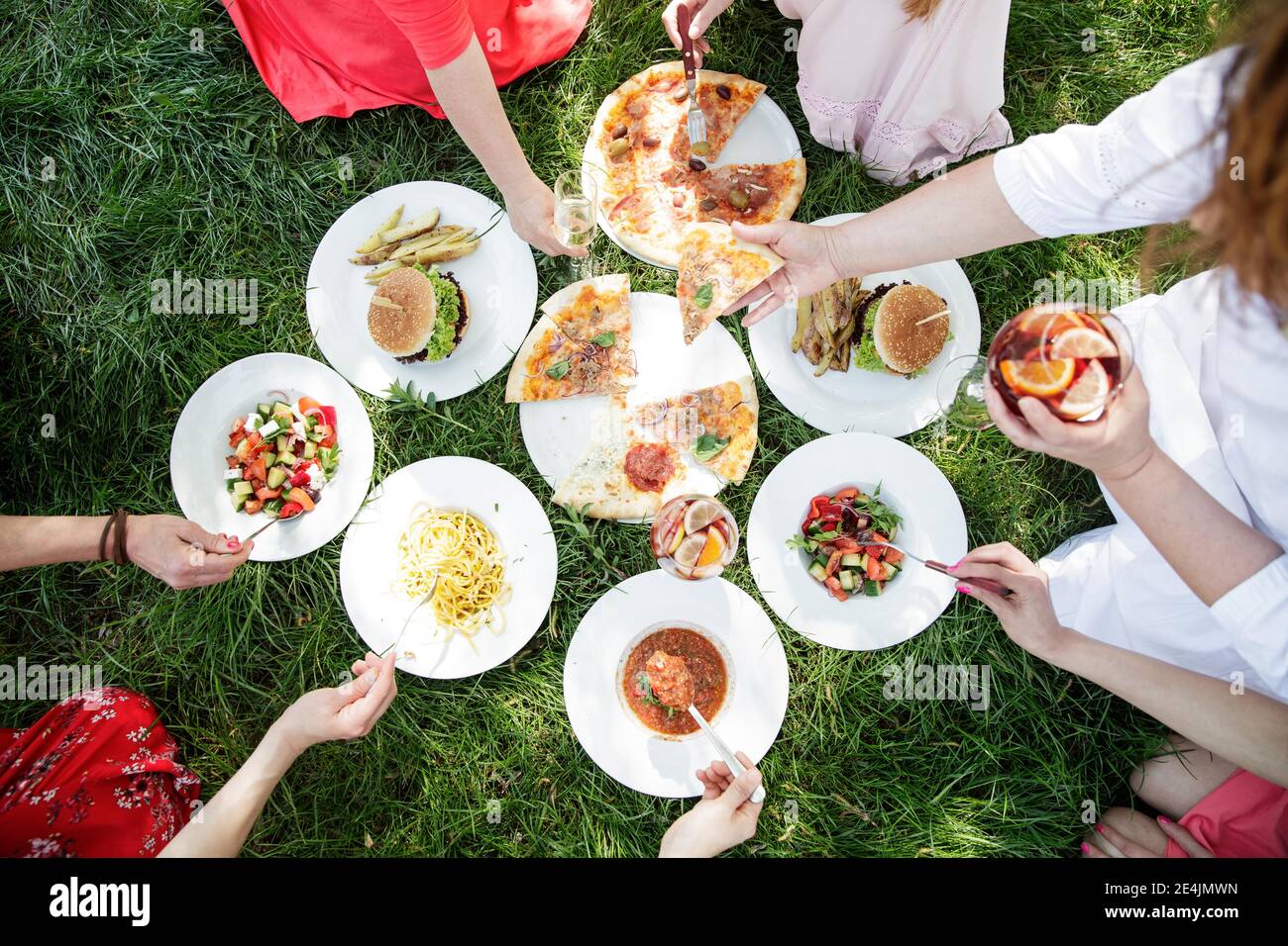 Group of women enjoying different food on grass, pizza, burger, salads ...