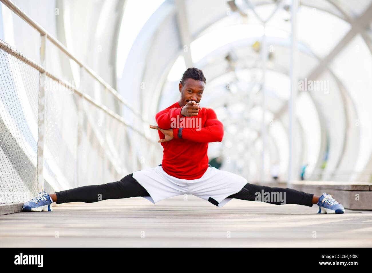 Male athlete pointing while stretching leg on walkway Stock Photo - Alamy