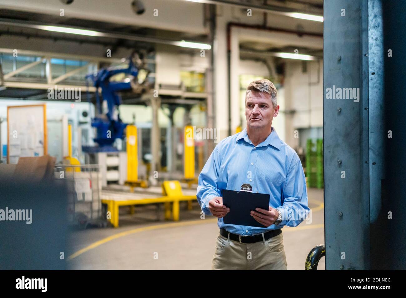Mature supervisor with clipboard looking away while working in factory ...